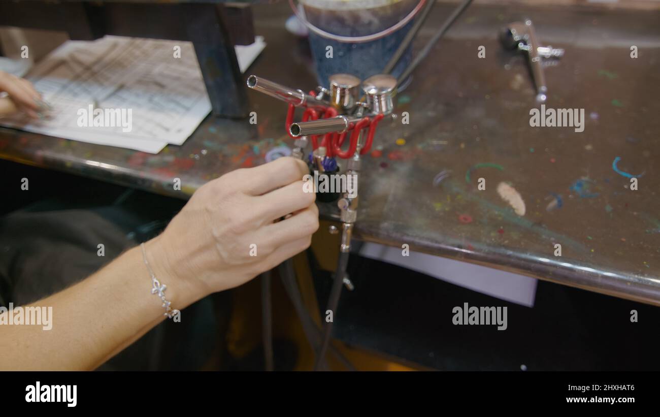 Woman artist learns to paint with airbrush with acrylic dye, paper and easel. Indoors. Concept ...