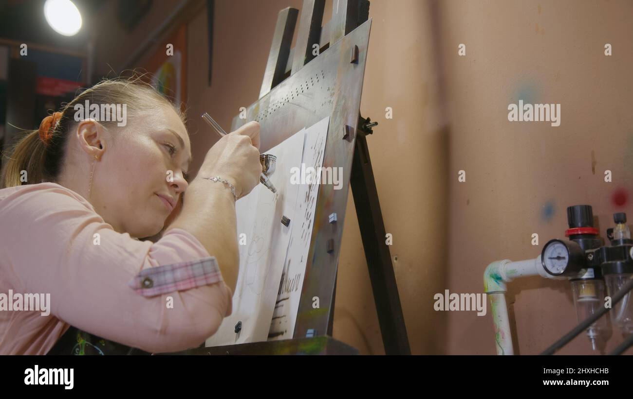 Woman artist learns to paint with airbrush with acrylic dye, paper and ...