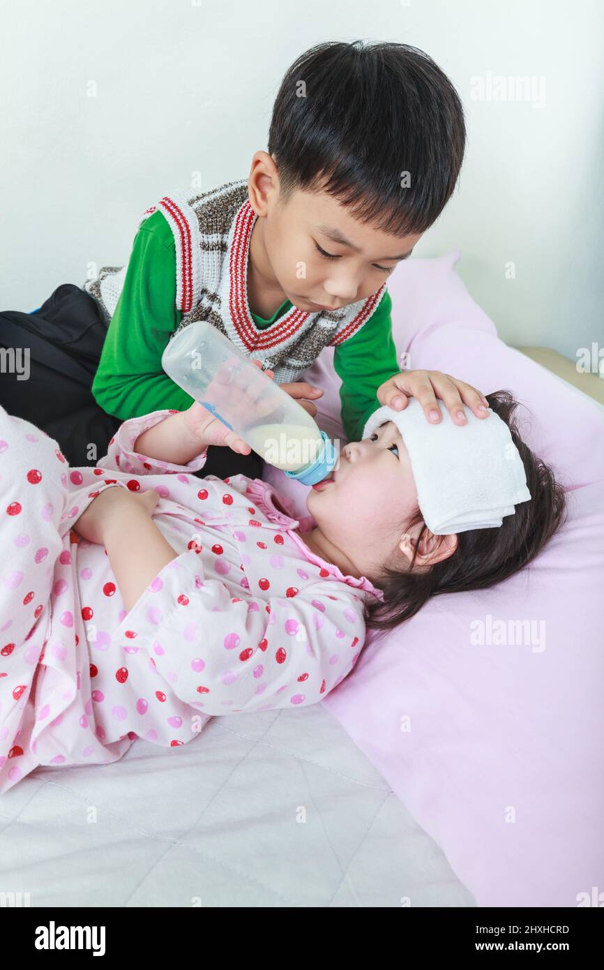 Sick sister lying and suck up milk on the bed, kindly brother keep ...