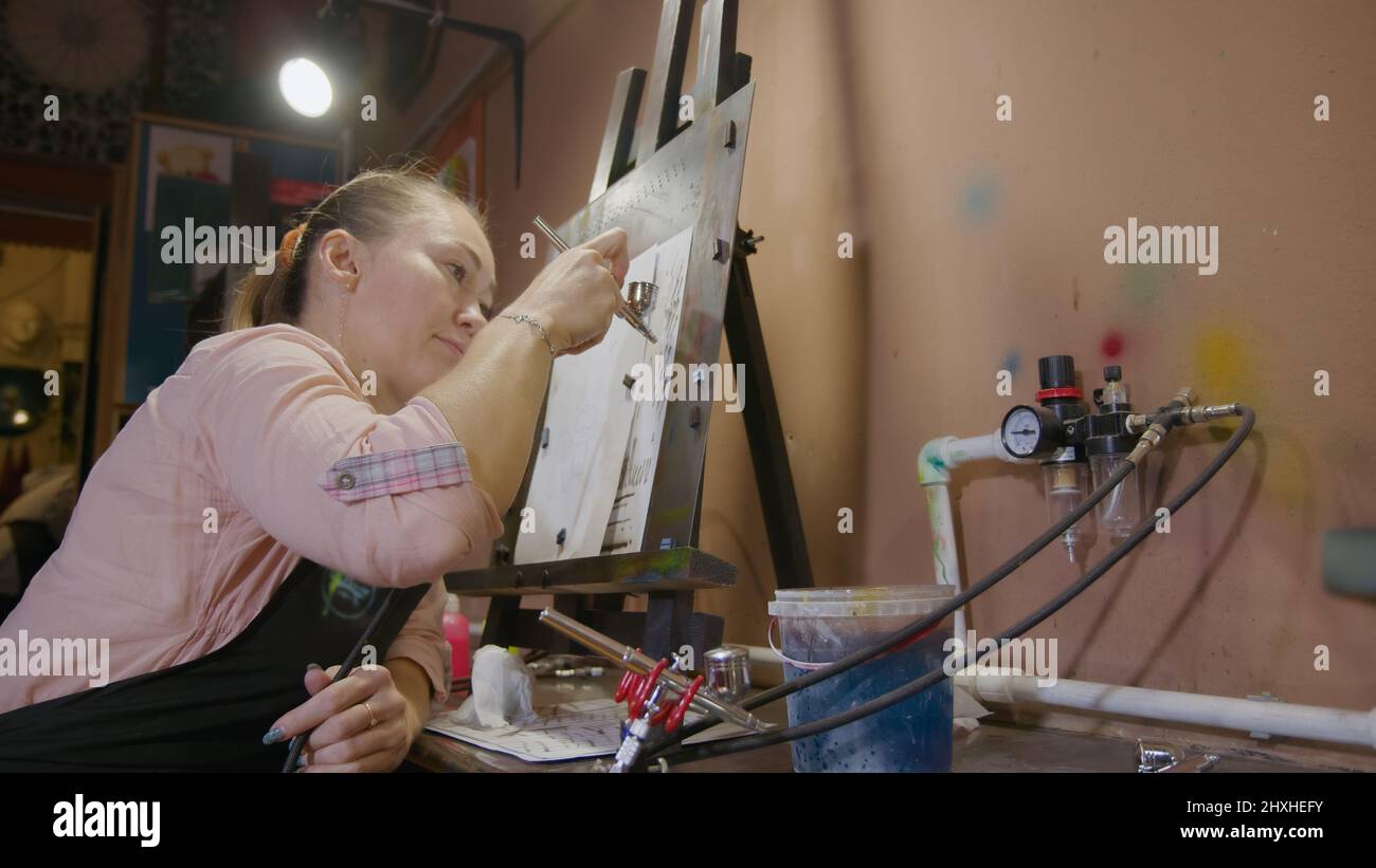 Woman artist learns to paint with airbrush with acrylic dye, paper and ...