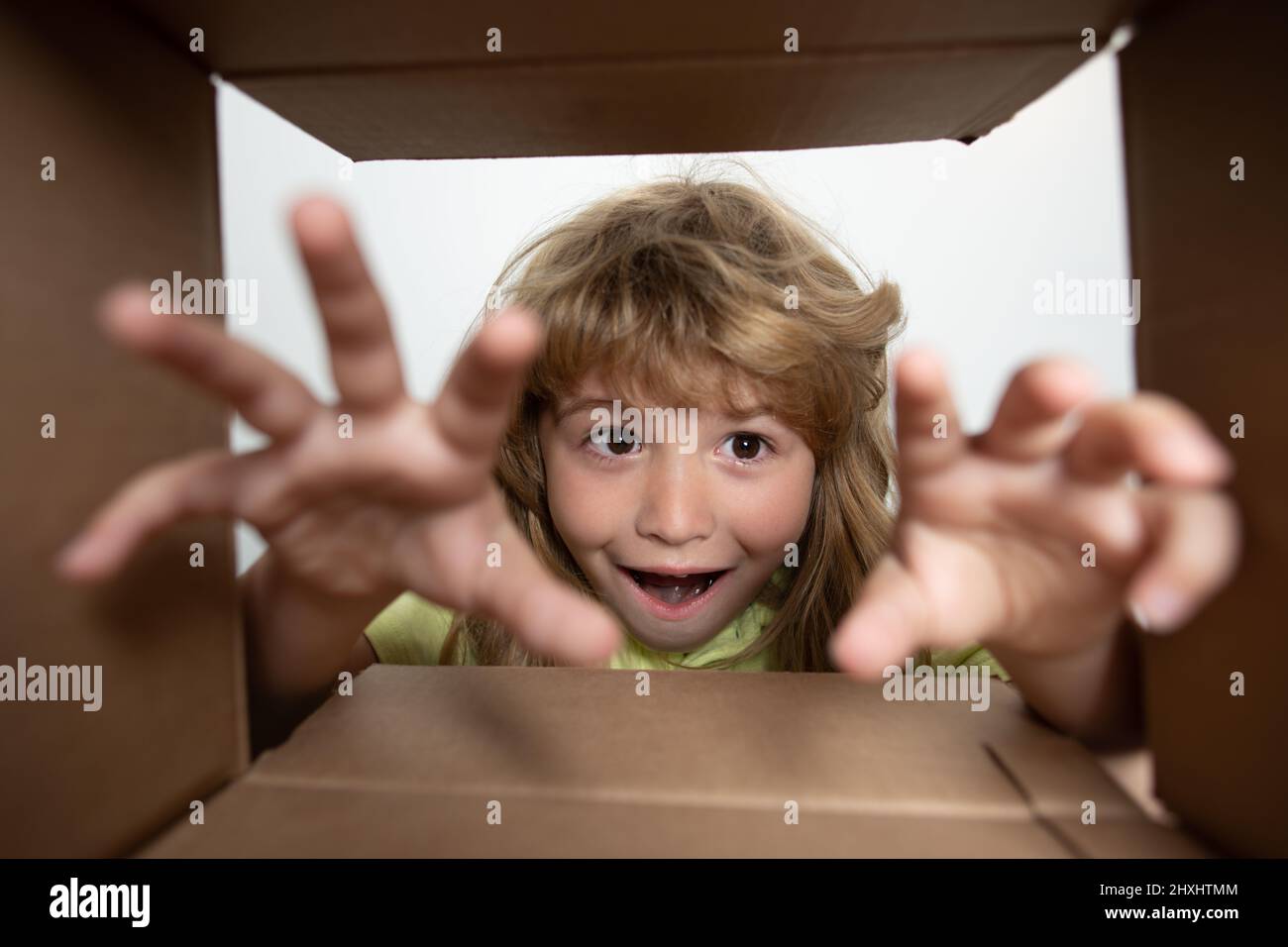 Funny excited child unpacking and opening the carton box looking inside ...