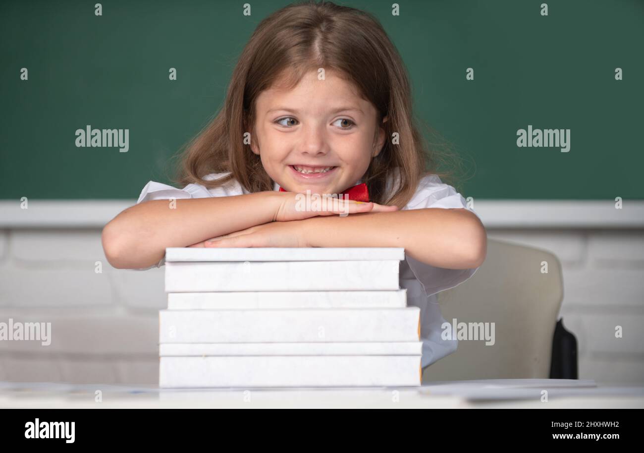 Smiling girl sitting at the desk and holding hands on the books in the ...