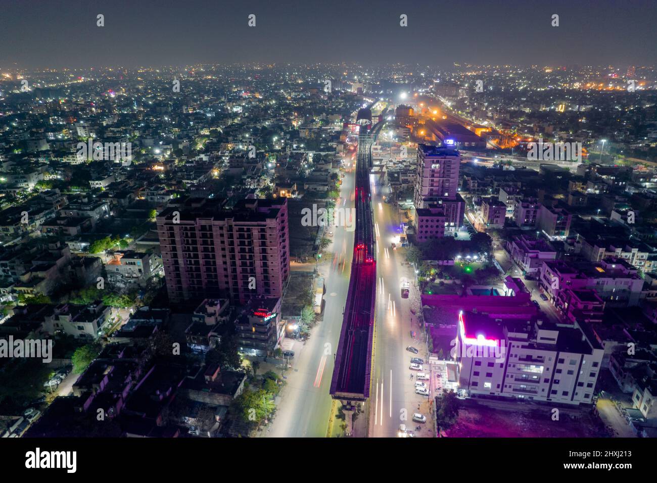 aerial drone shot showing elevated metro track over lit road surrounded ...