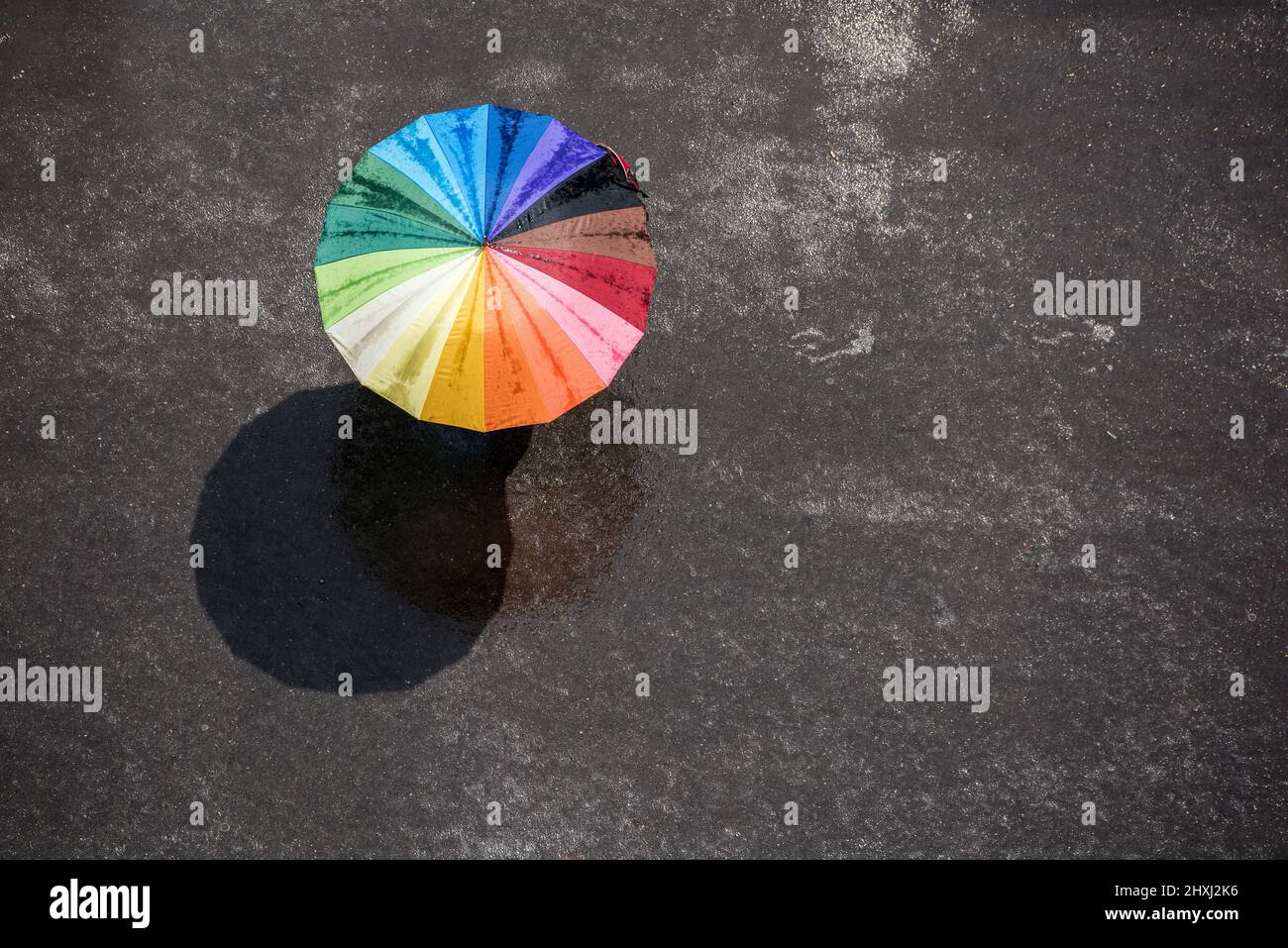 People shelter under an multicolored umbrella in the rain. Above view ...