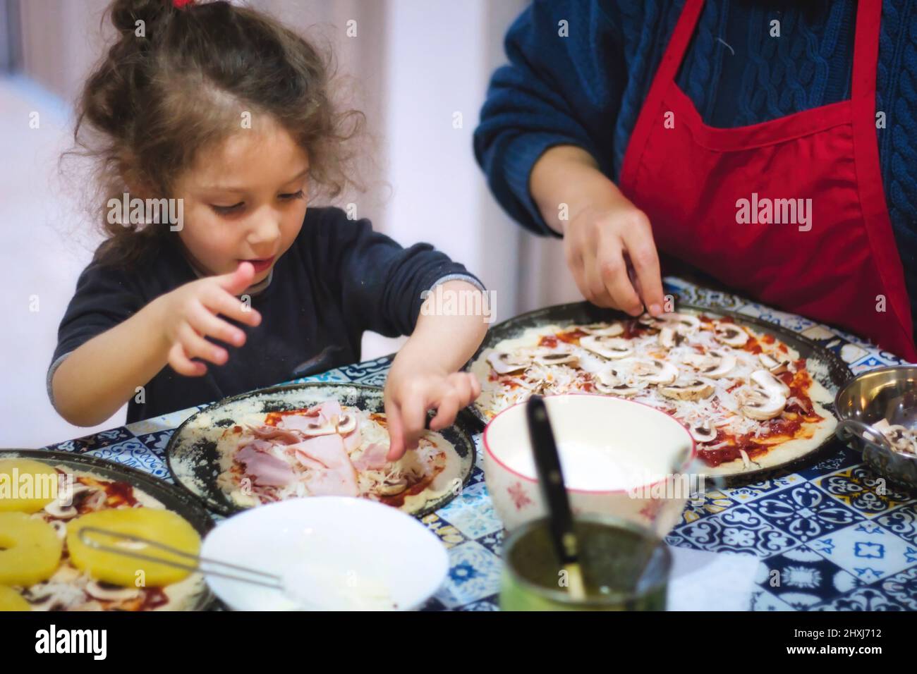 Young girl and mother making homemade pizzas in a domestic kitchen ...