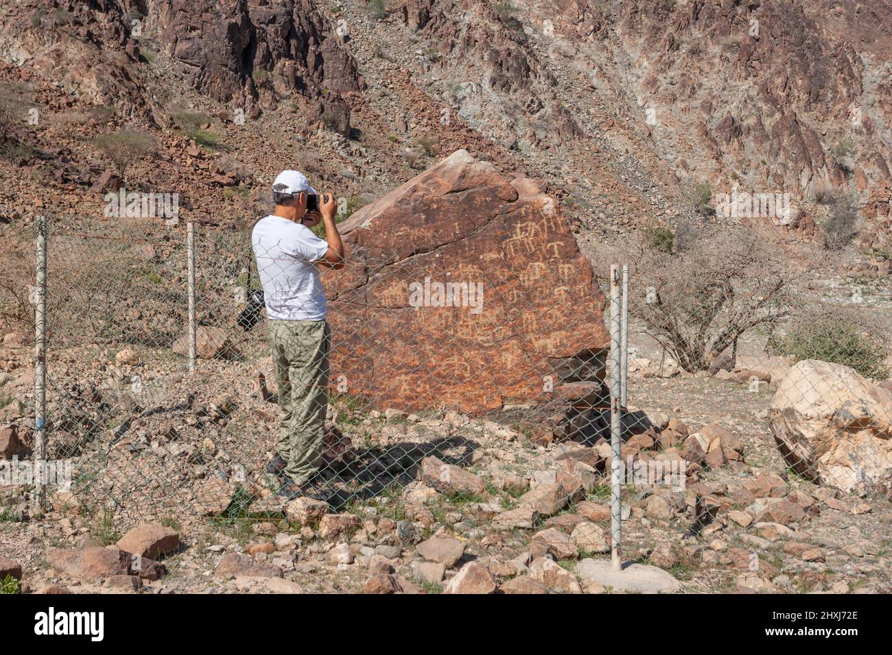 An unidentified man photographing a rock bearing petroglyphs in Wadi ...