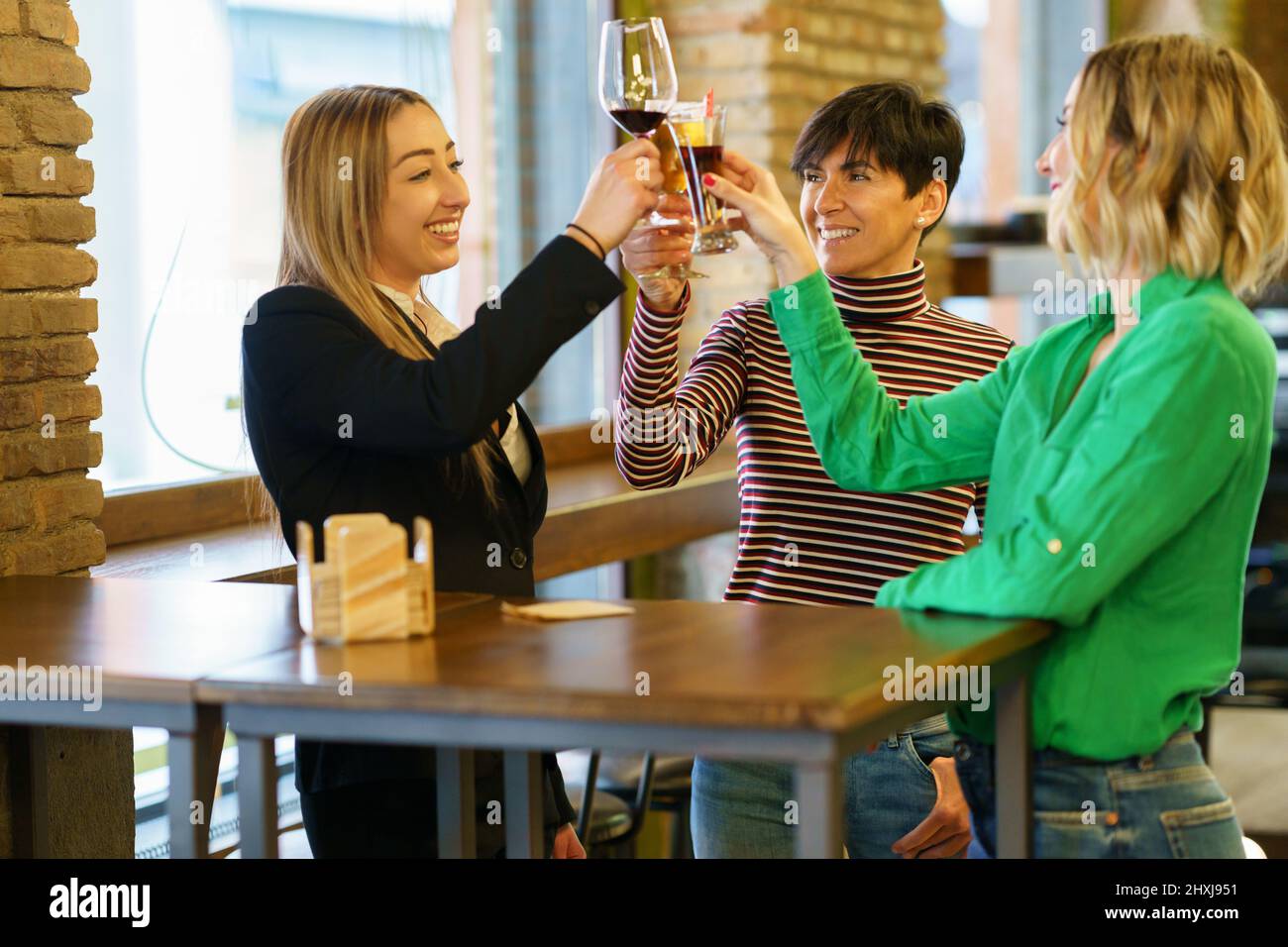 Excited women proposing toast near pub window Stock Photo - Alamy