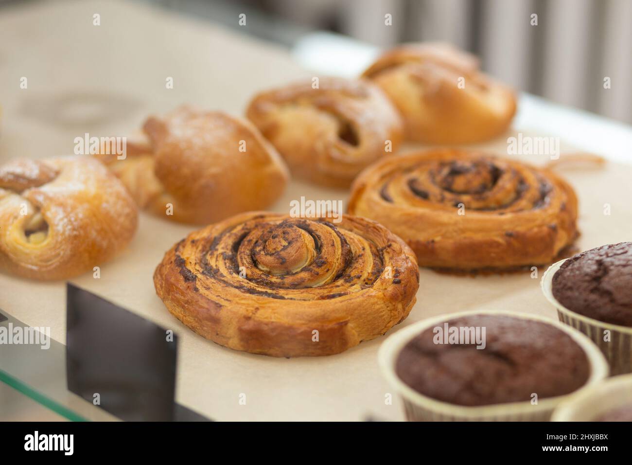 Variety baked muffins and buns in glass showcase at bakery cafe. Donuts ...