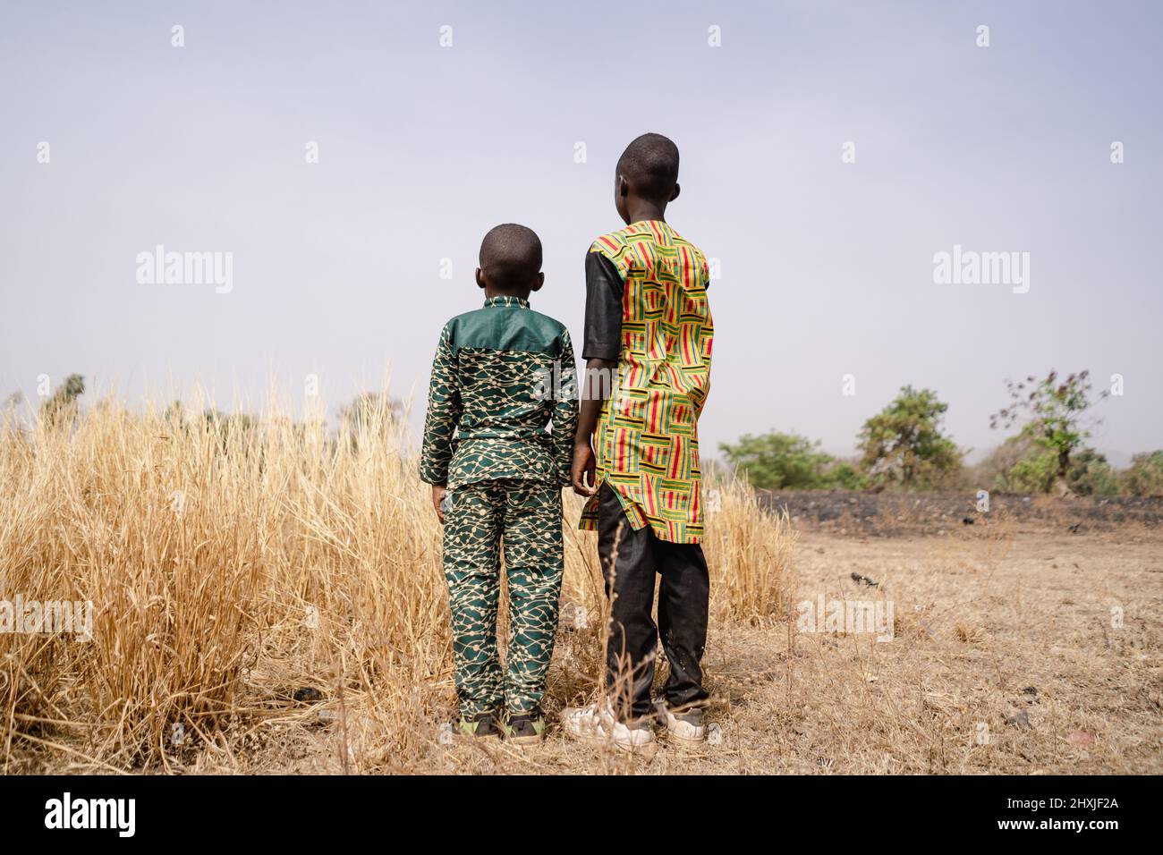 Rear view of two African boys standing in front of a barren field with ...