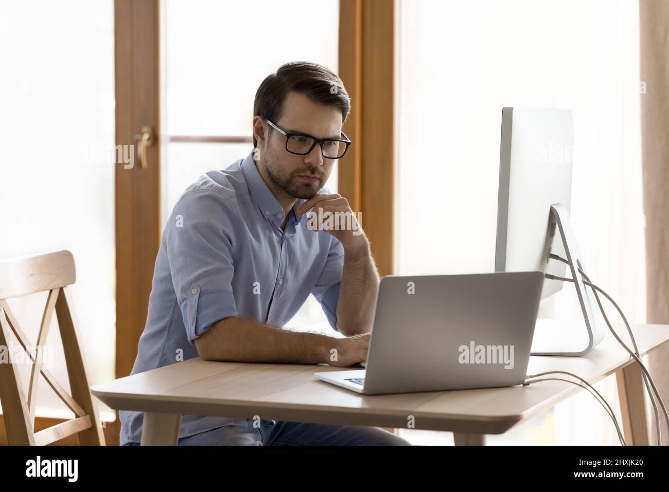 Serious young man work from home office on two computers Stock Photo ...