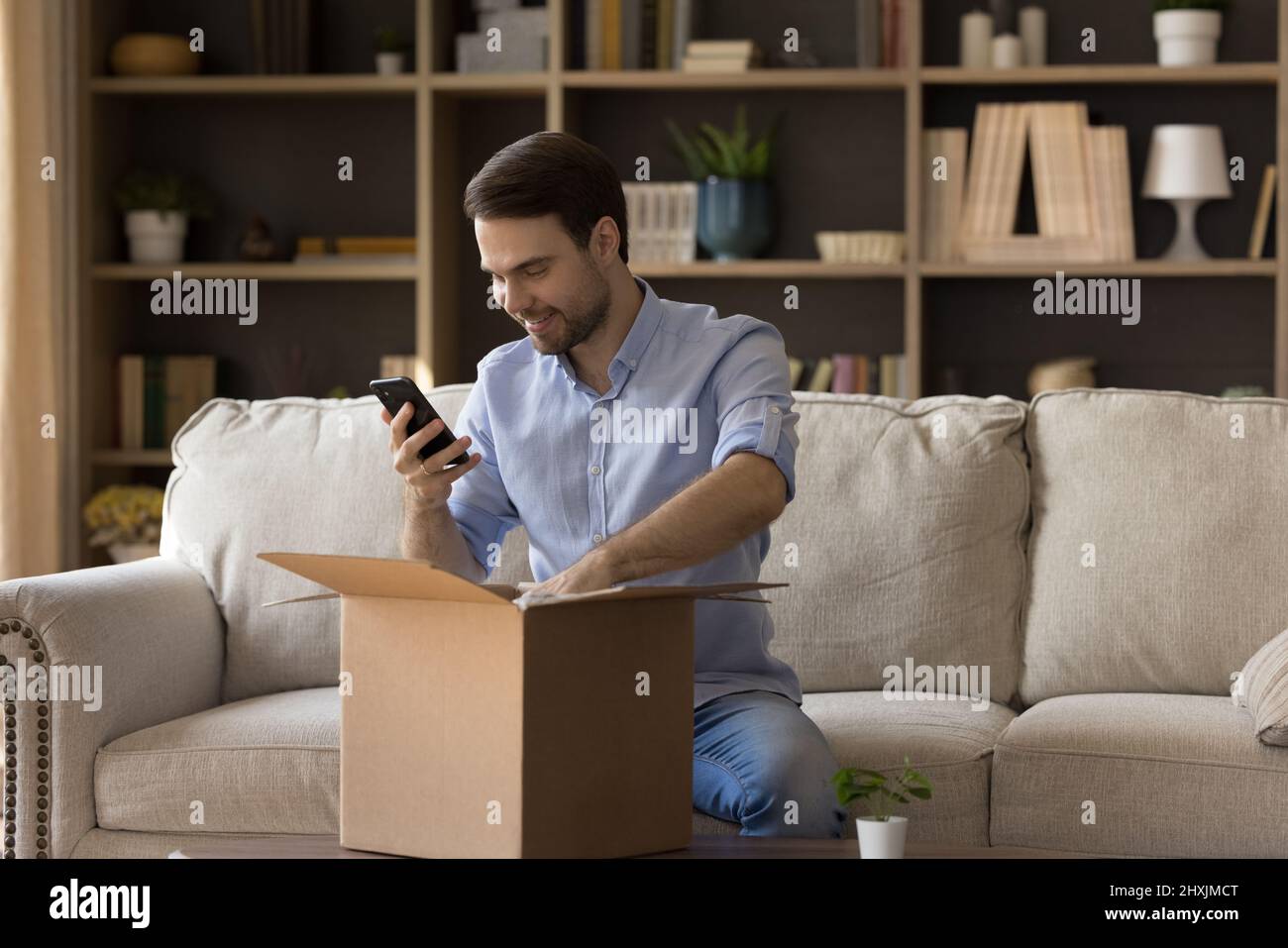 Happy young male open postal parcel make photo on phone Stock Photo - Alamy