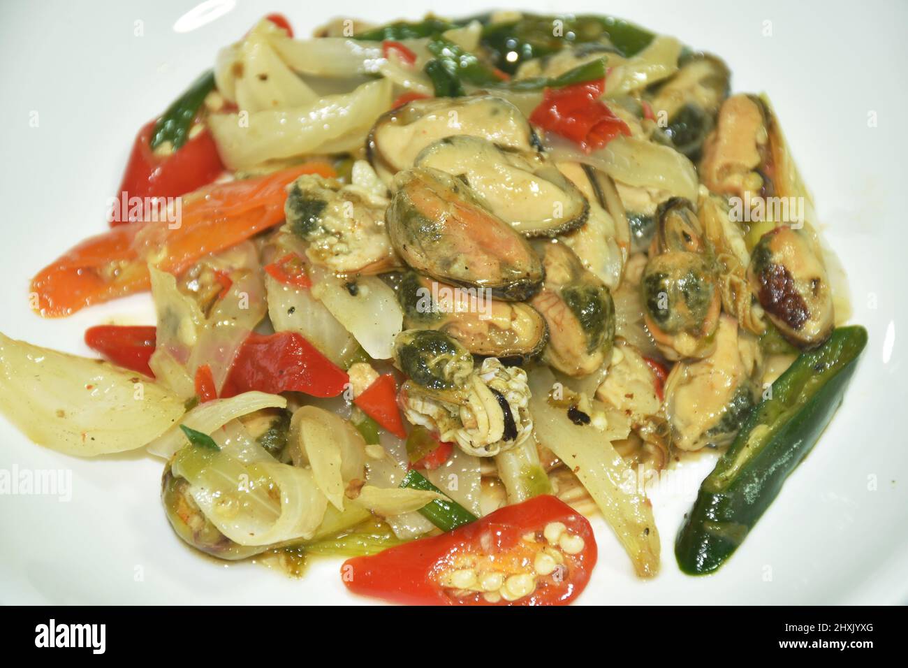spicy stir fried mussel with slice onion and basil leaf on plate Stock ...