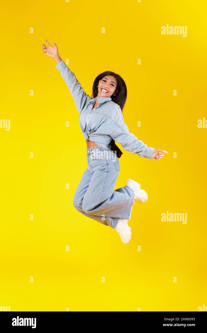 Excited young woman jumping up at orange studio Stock Photo - Alamy