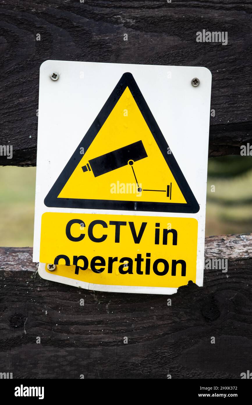 Broken yellow cctv in operation warning sign on a wooden fence Stock ...