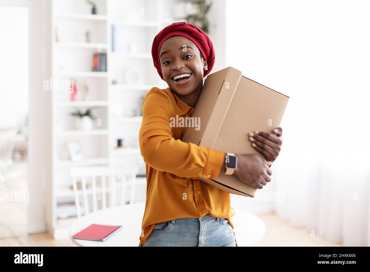 Ecstatic young black woman hugging box at home Stock Photo - Alamy