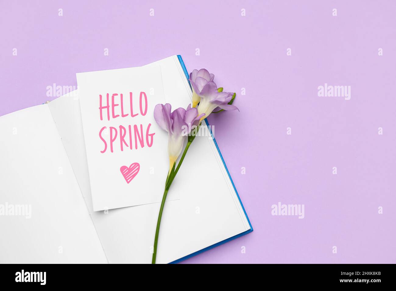 Card with text HELLO SPRING, notebook and freesia flower on lilac ...