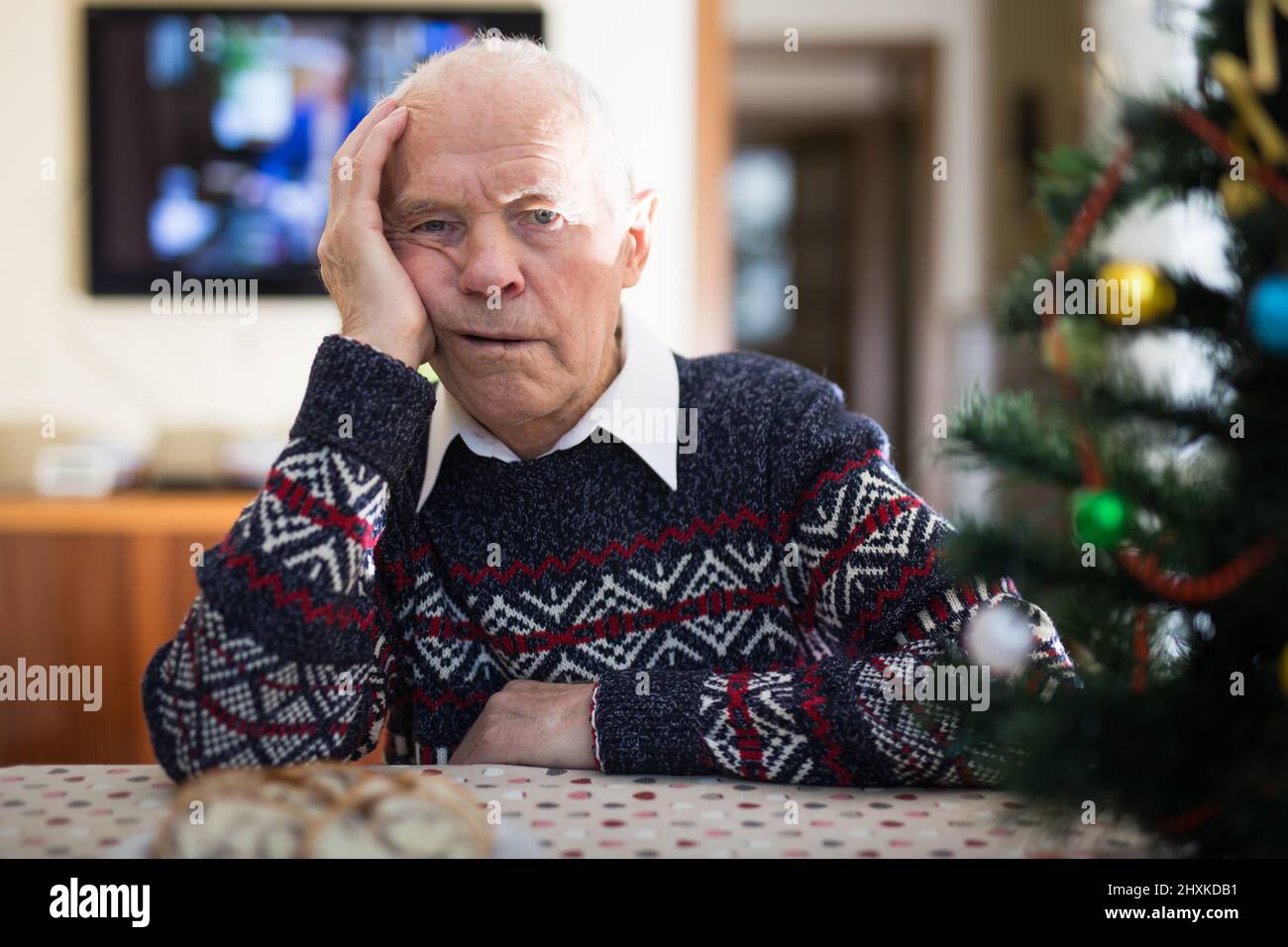 Sad bored elderly man sitting alone at home table with decorated small ...
