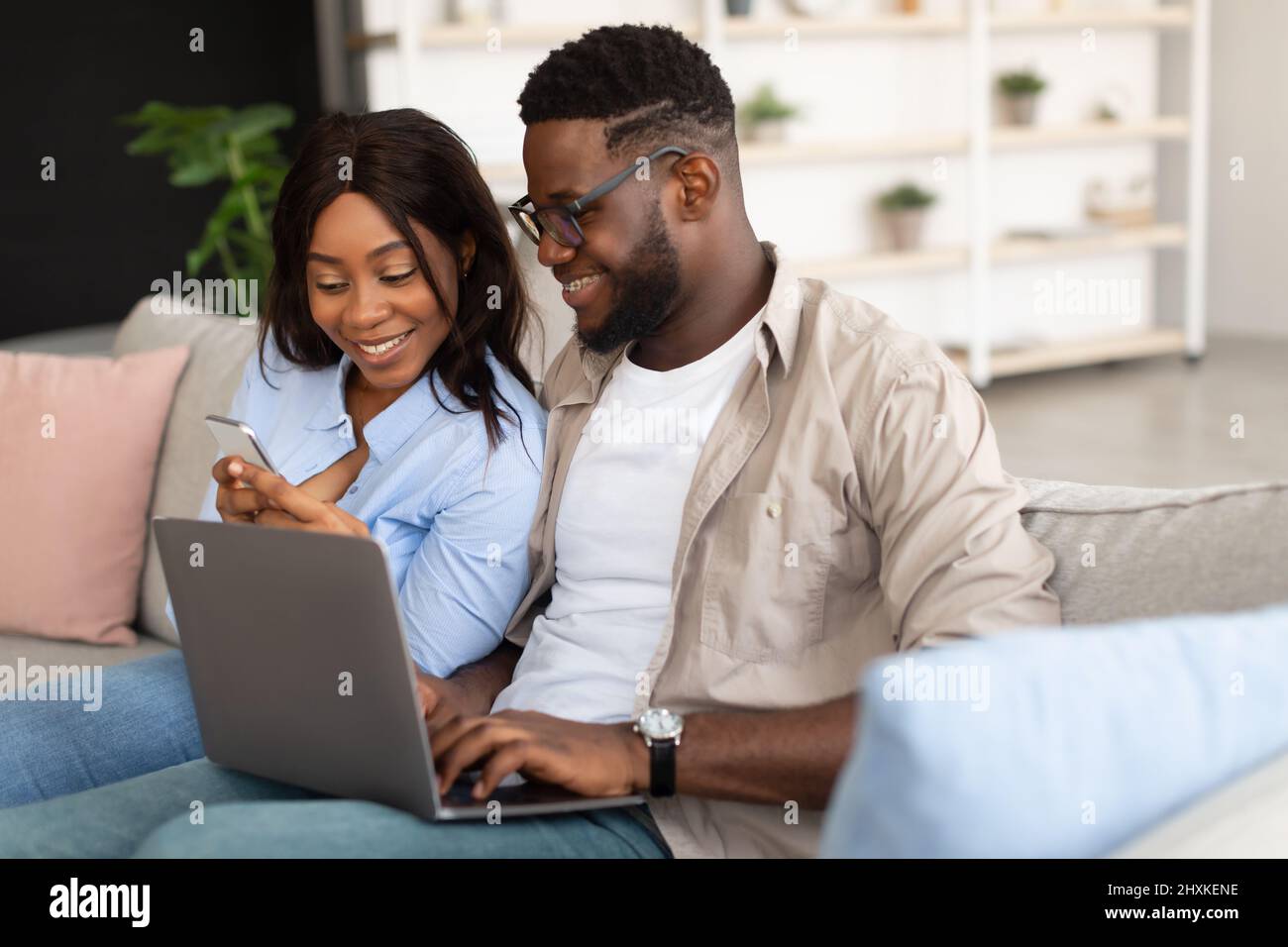 Happy black couple sitting on couch, using cellphone and pc Stock Photo ...