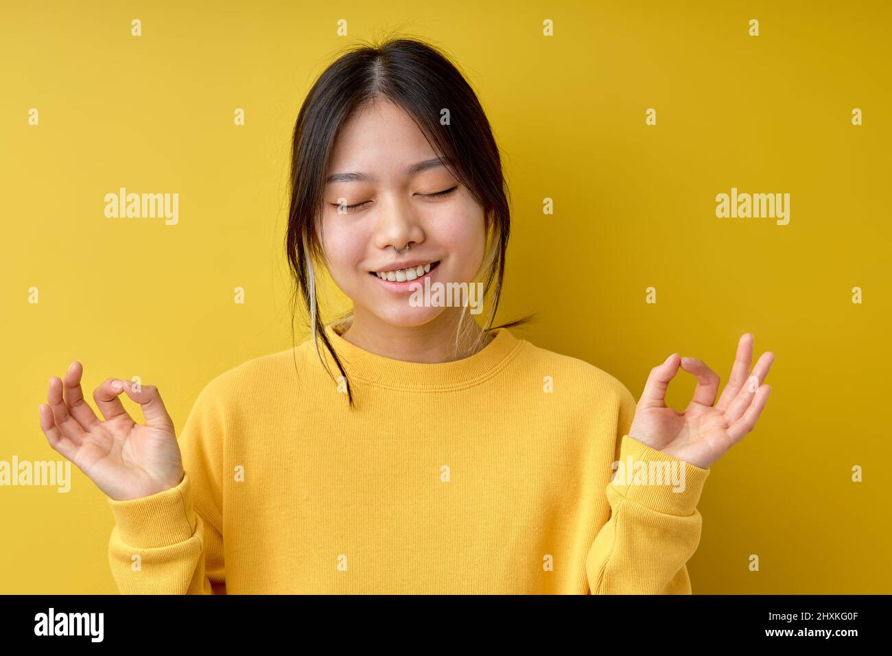 Beautiful cheerful chinese woman meditating over yellow isolated ...