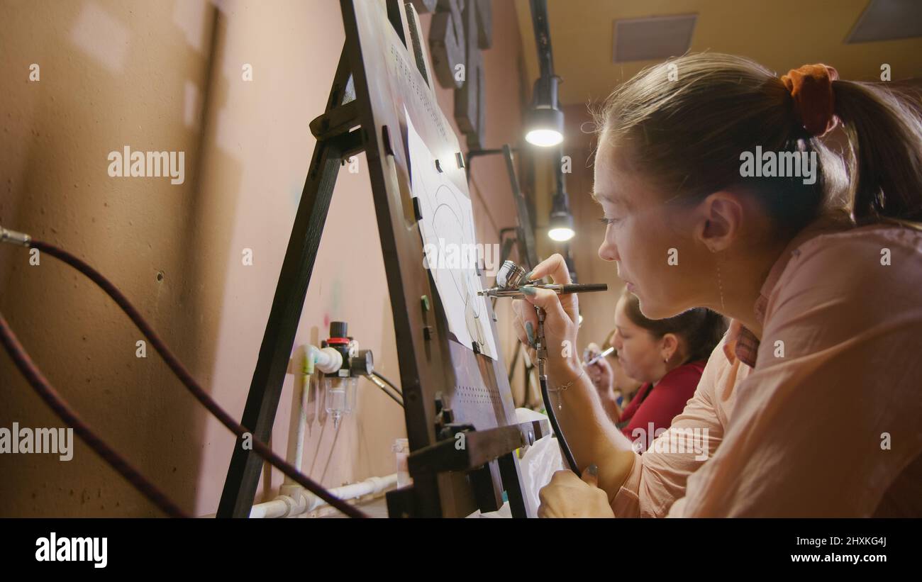 Woman artist learns to paint with airbrush with acrylic dye, paper and ...