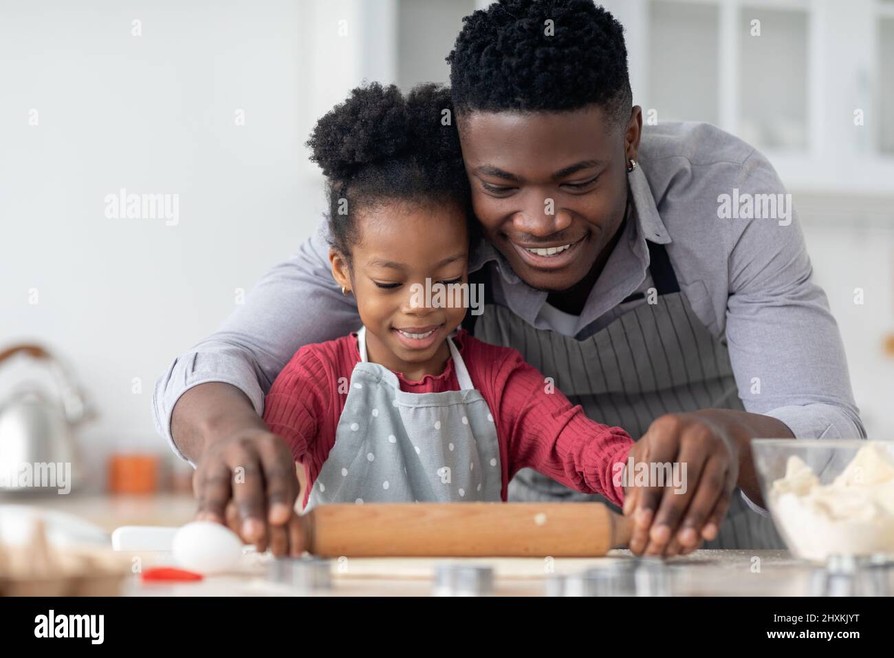 Black father and daughter rolling pastry dough and smiling Stock Photo ...