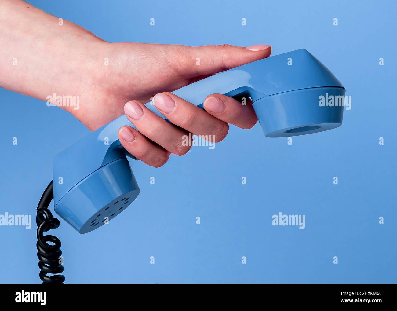 Hand holding retro phone receiver on blue background Stock Photo - Alamy