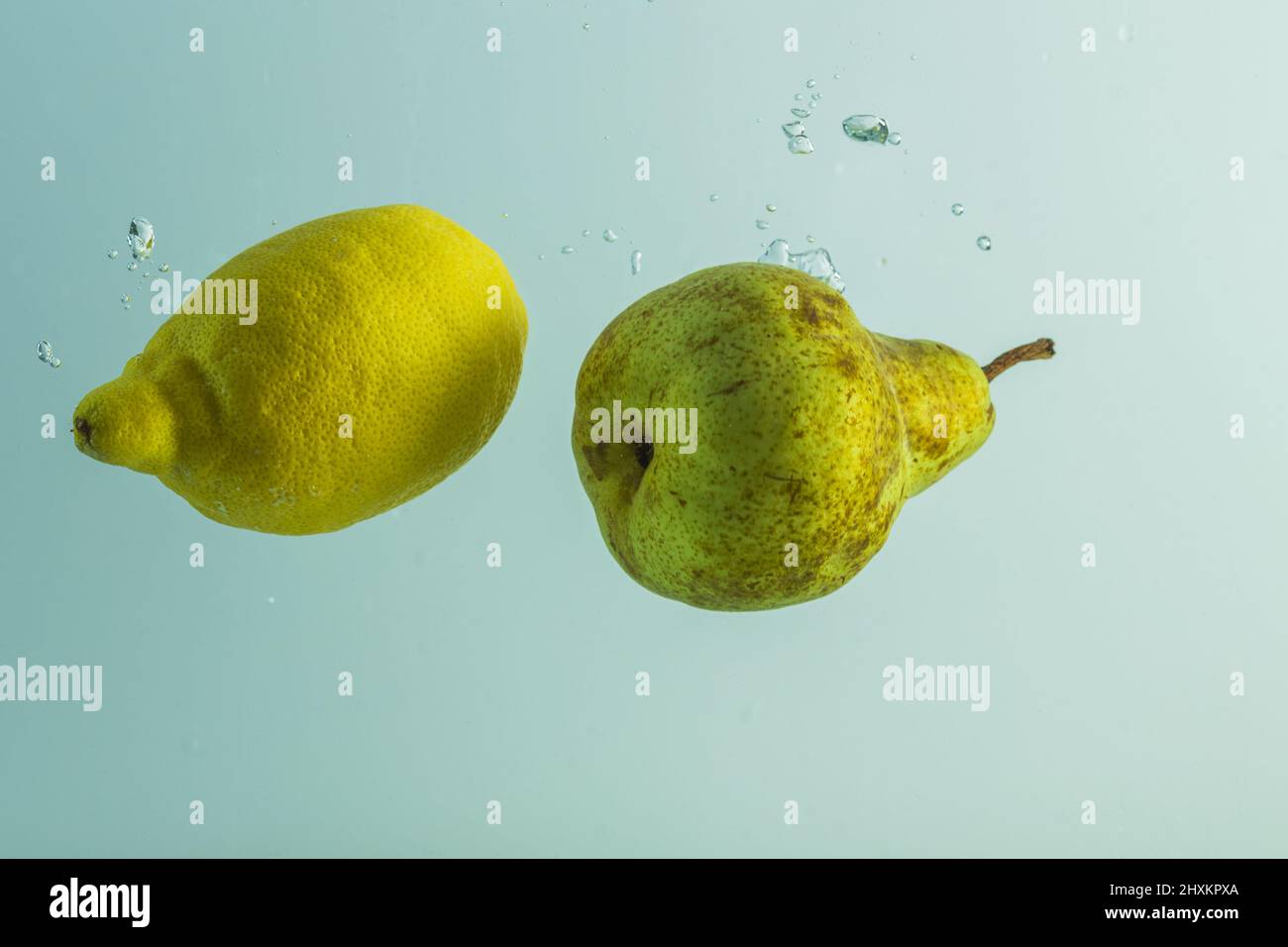Close up view of falling lemon and pear into water. Healthy food ...