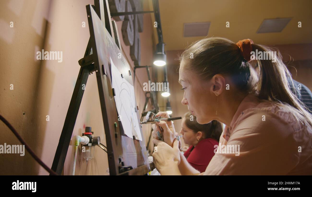 Woman artist learns to paint with airbrush with acrylic dye, paper and ...