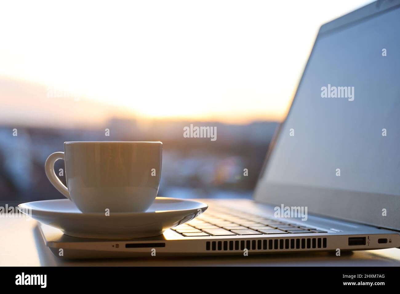 Coffee cup and saucer on laptop against the window with sunshine. Cozy ...