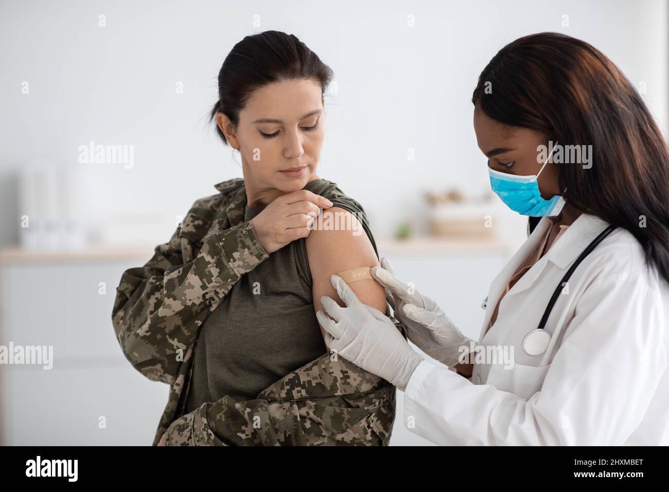 Black Female Doctor Applying Plaster On Soldier Woman's Shoulder After ...