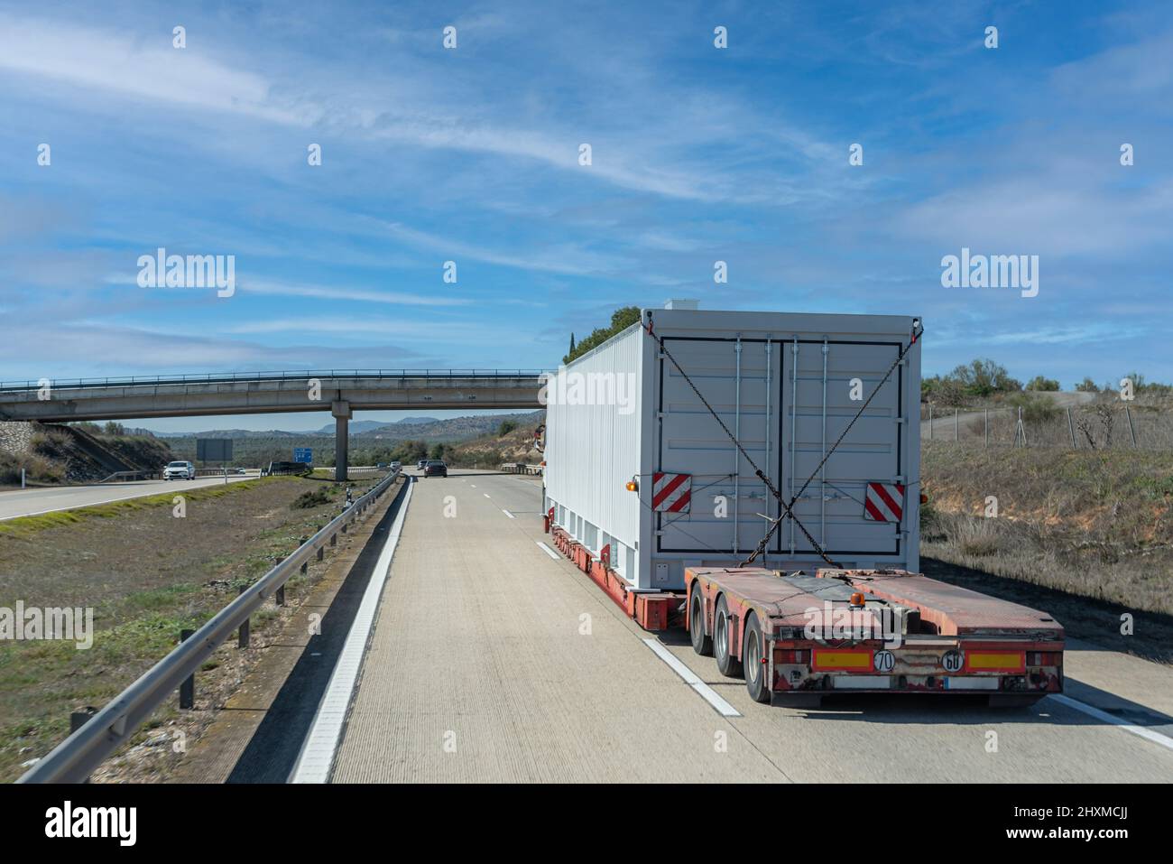 Platform truck loaded with a huge container that, due to its size, is ...