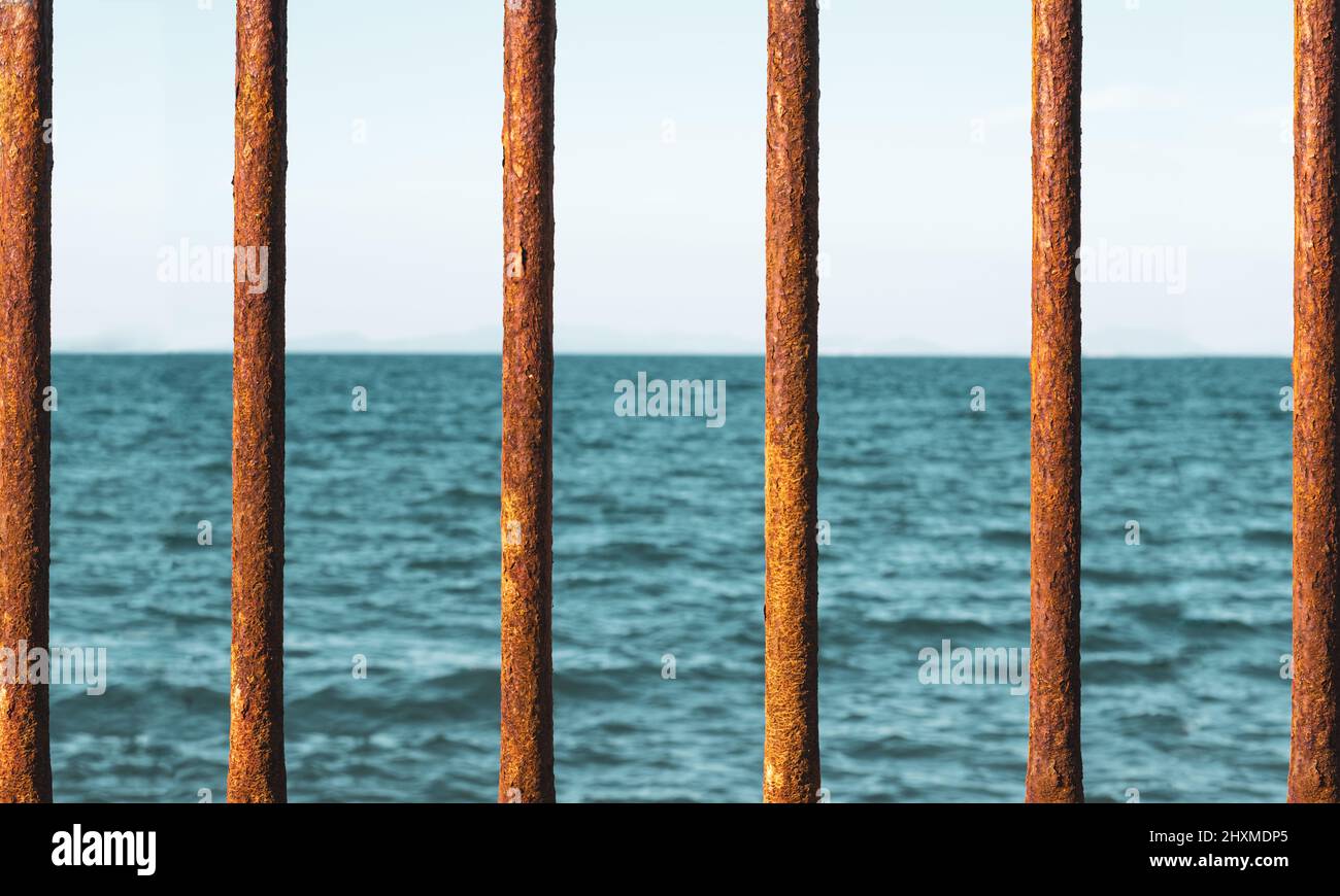 Rusty iron railing of a prison with beautiful sea and white sky ...