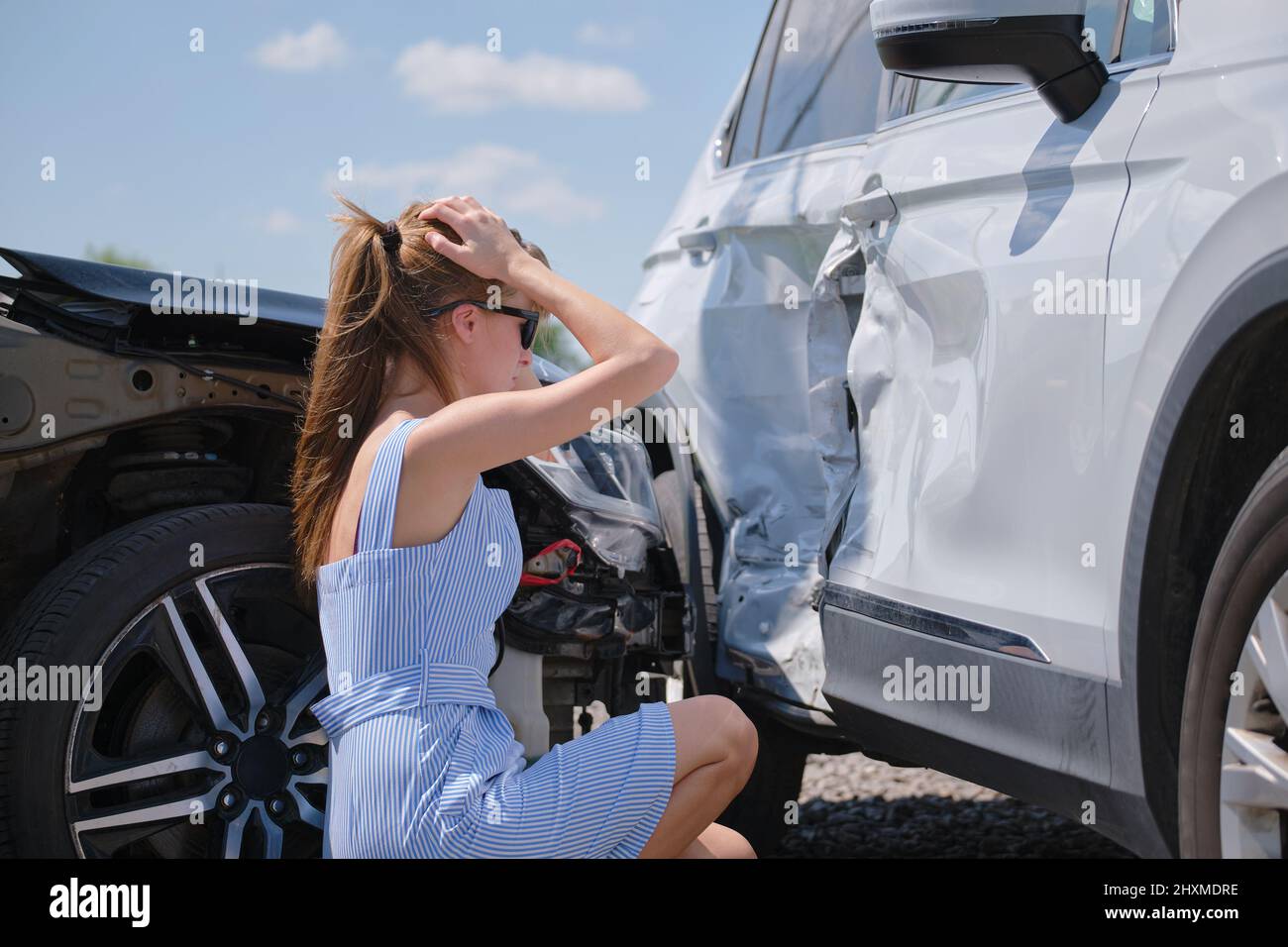 Sad young woman driver sitting near her smashed car looking shocked on ...