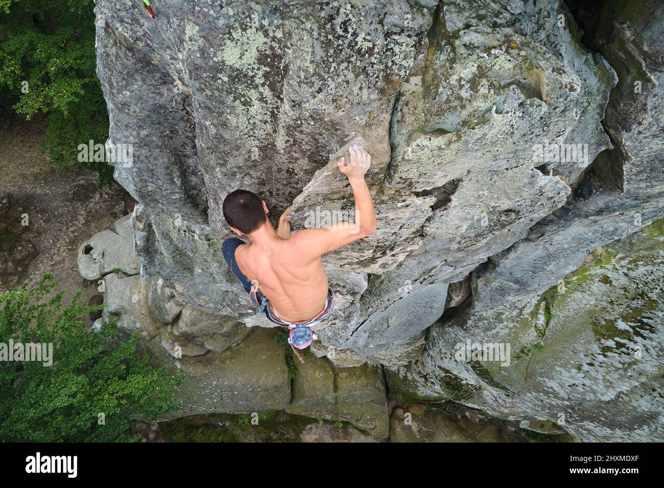 Young man climbing steep wall of rocky mountain. Male climber overcomes ...