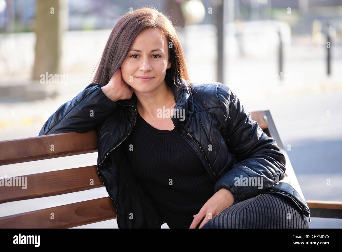 Young happy woman sitting relaxed on street bench on warm autunm day ...