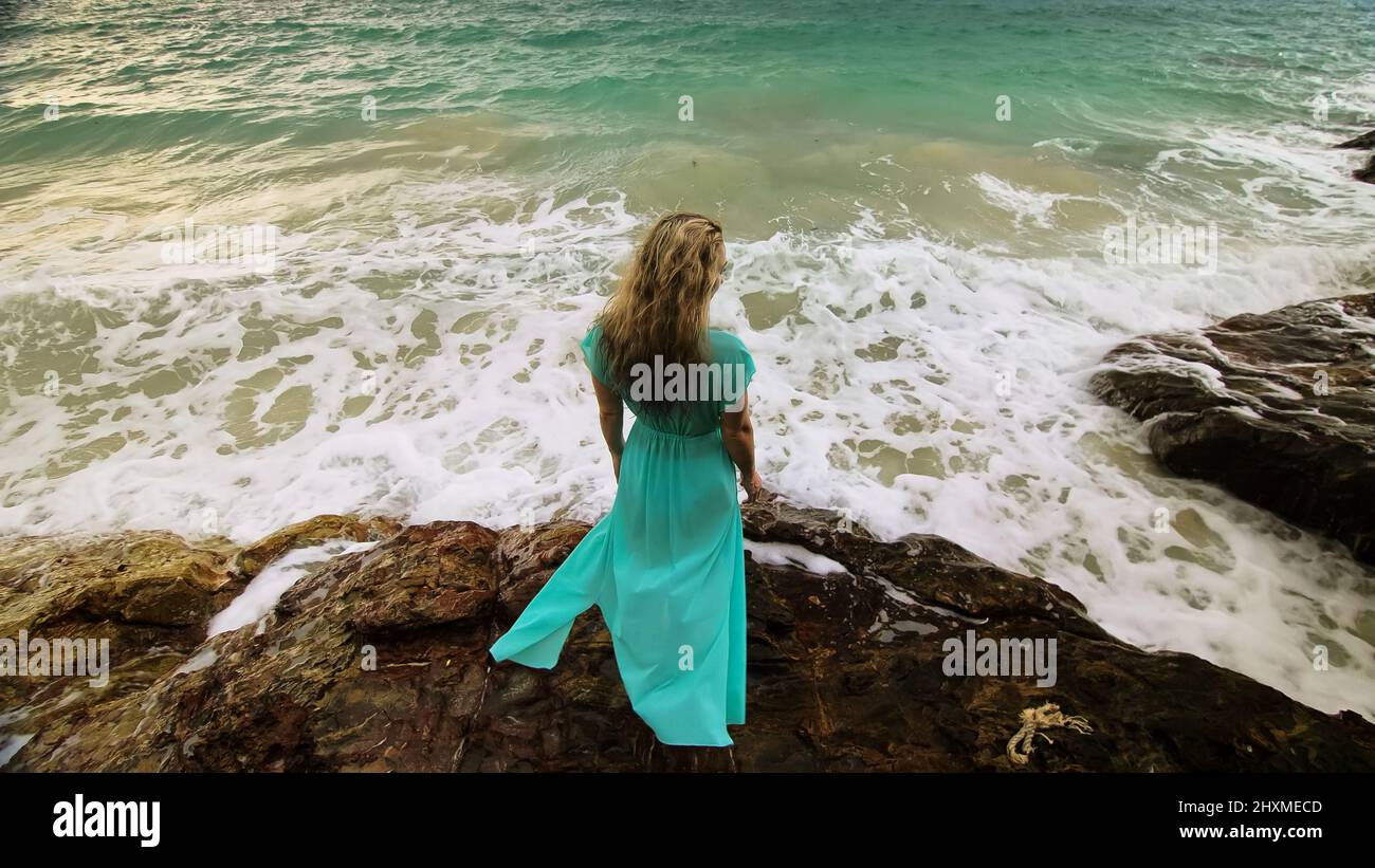 Seductive long-haired woman walks on rock of sea reef stone, stormy ...