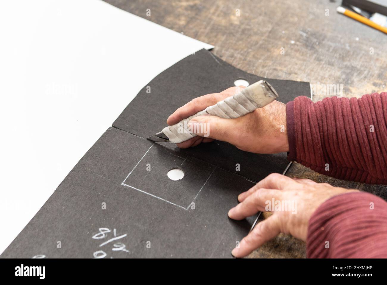 Skilled hands make the precise cuts with a razor on the leather pattern template to create a new ...