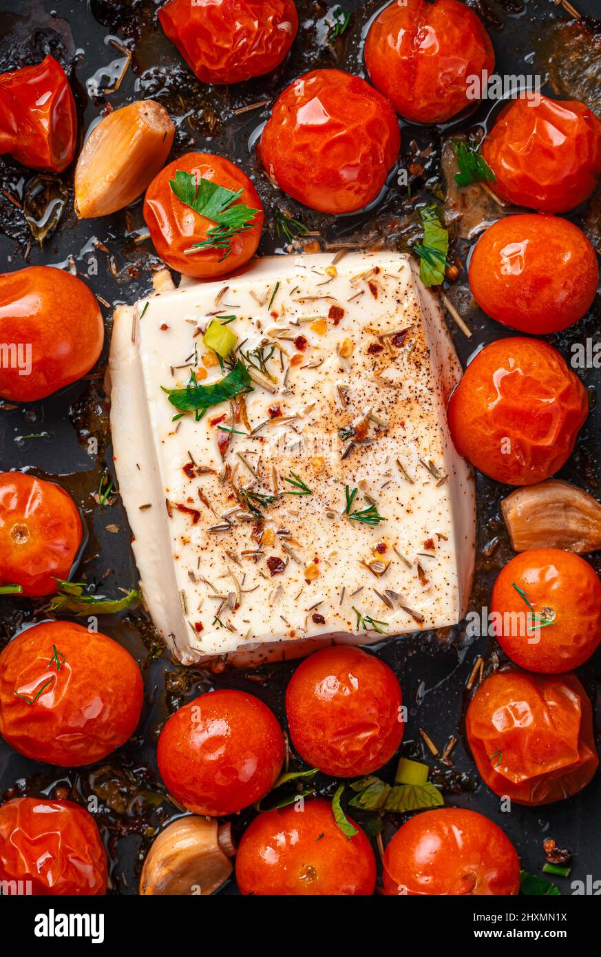 Oven-baked feta cheese with cherry tomatoes and herbs close-up. Top ...