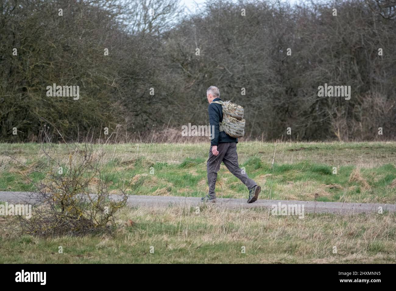 man with a laden backpack walking at speed along an unmade track road ...