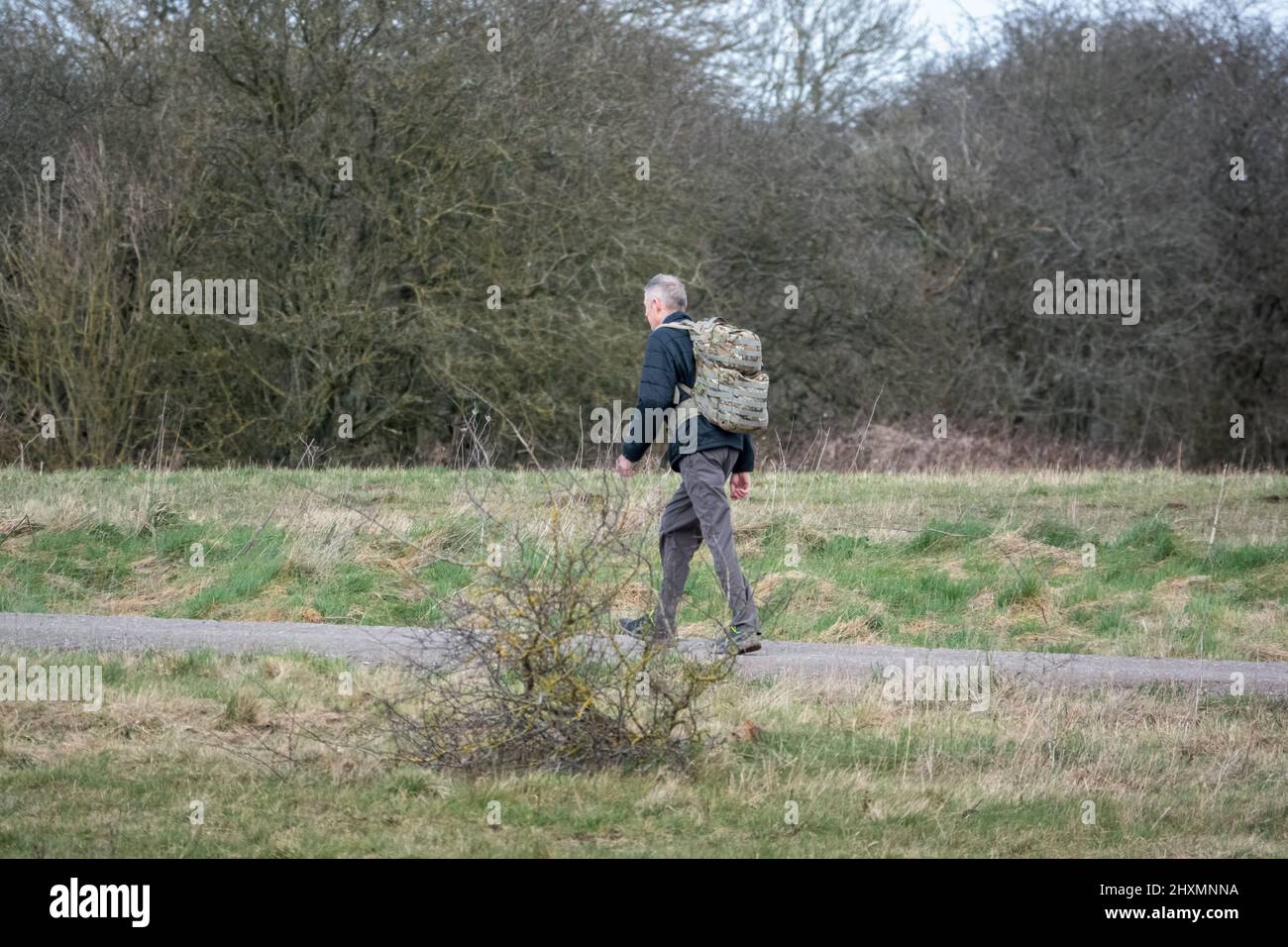 man with a laden backpack walking at speed along an unmade track road ...