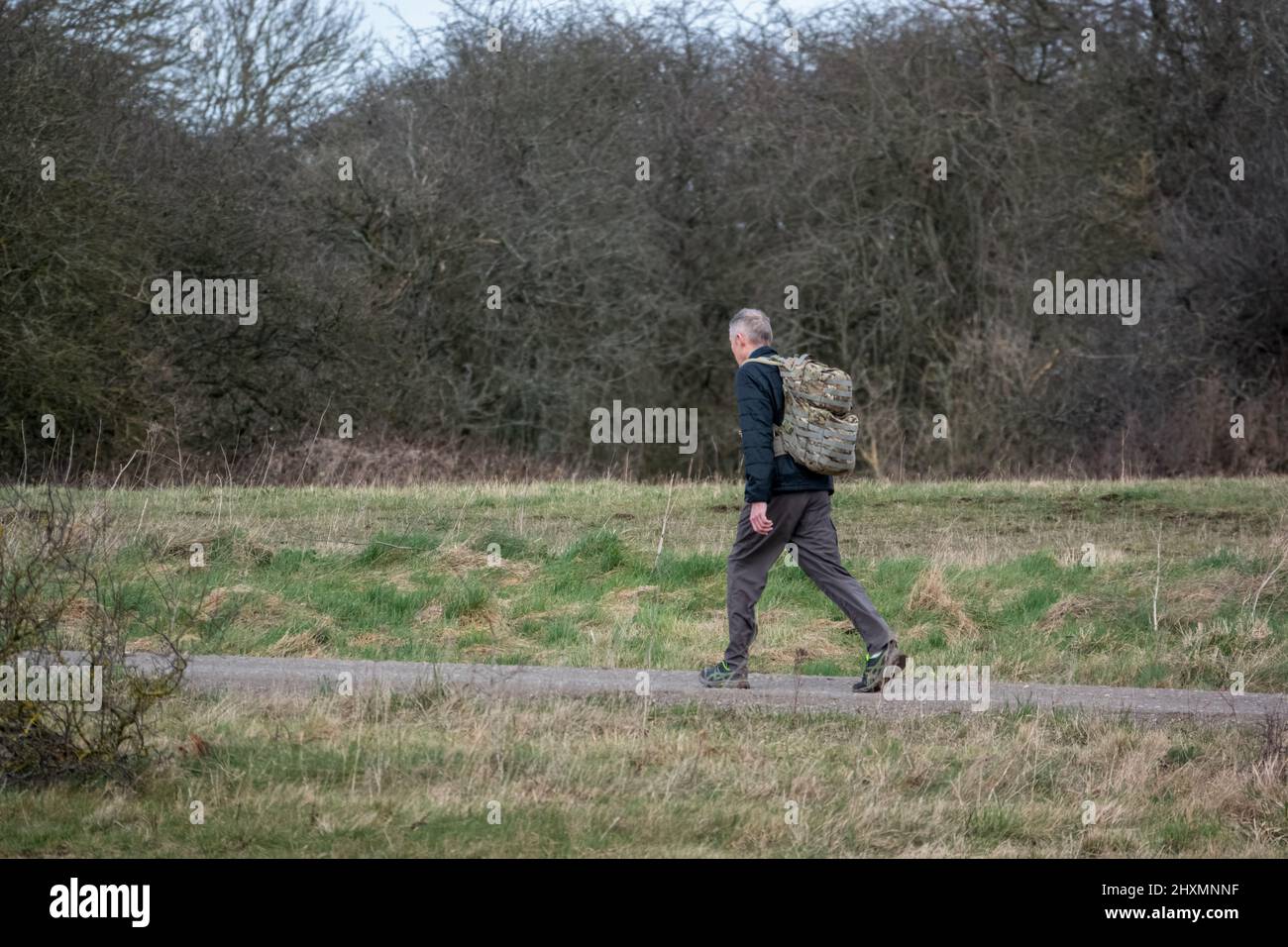 man with a laden backpack walking at speed along an unmade track road ...