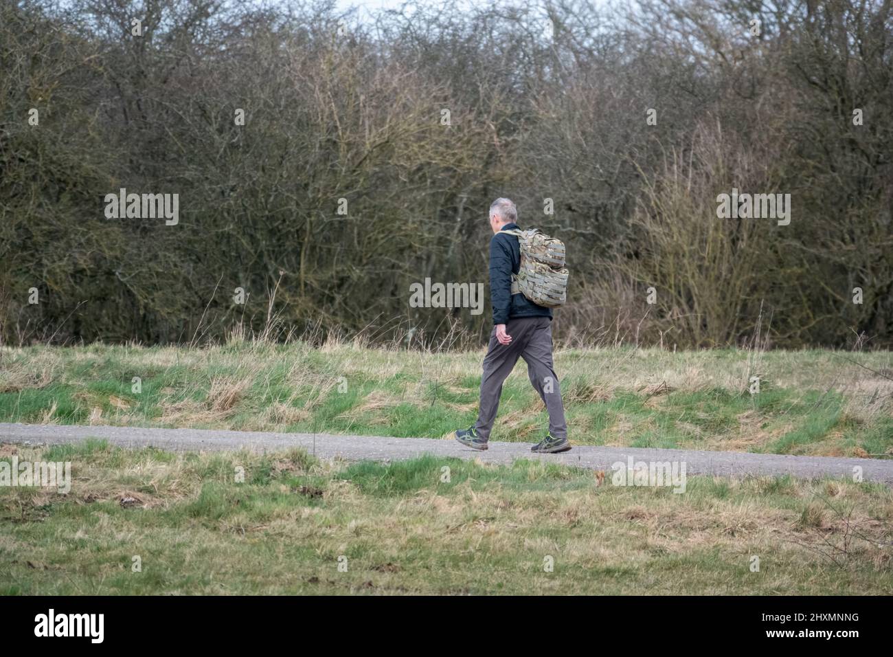 man with a laden backpack walking at speed along an unmade track road ...