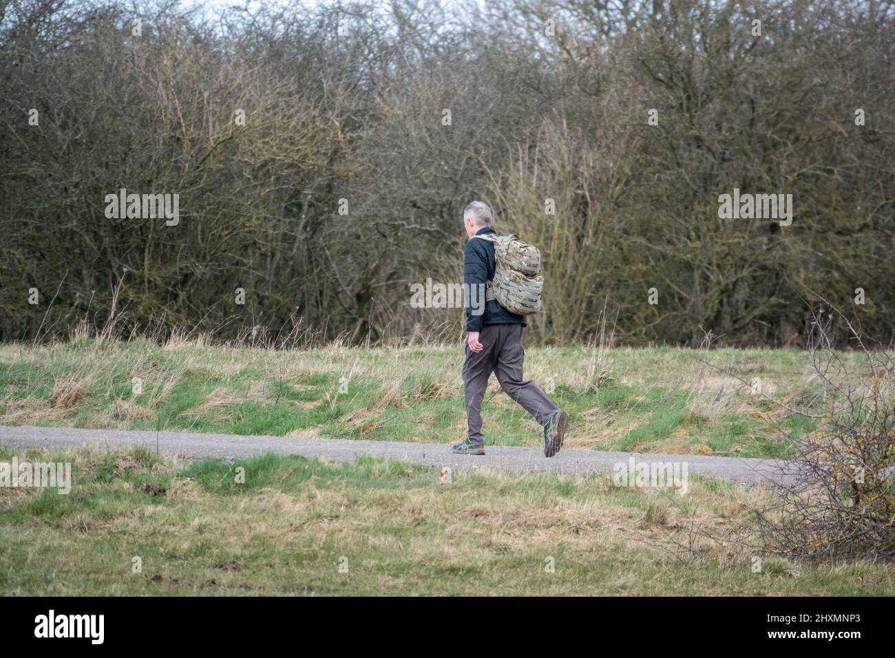 man with a laden backpack walking at speed along an unmade track road ...