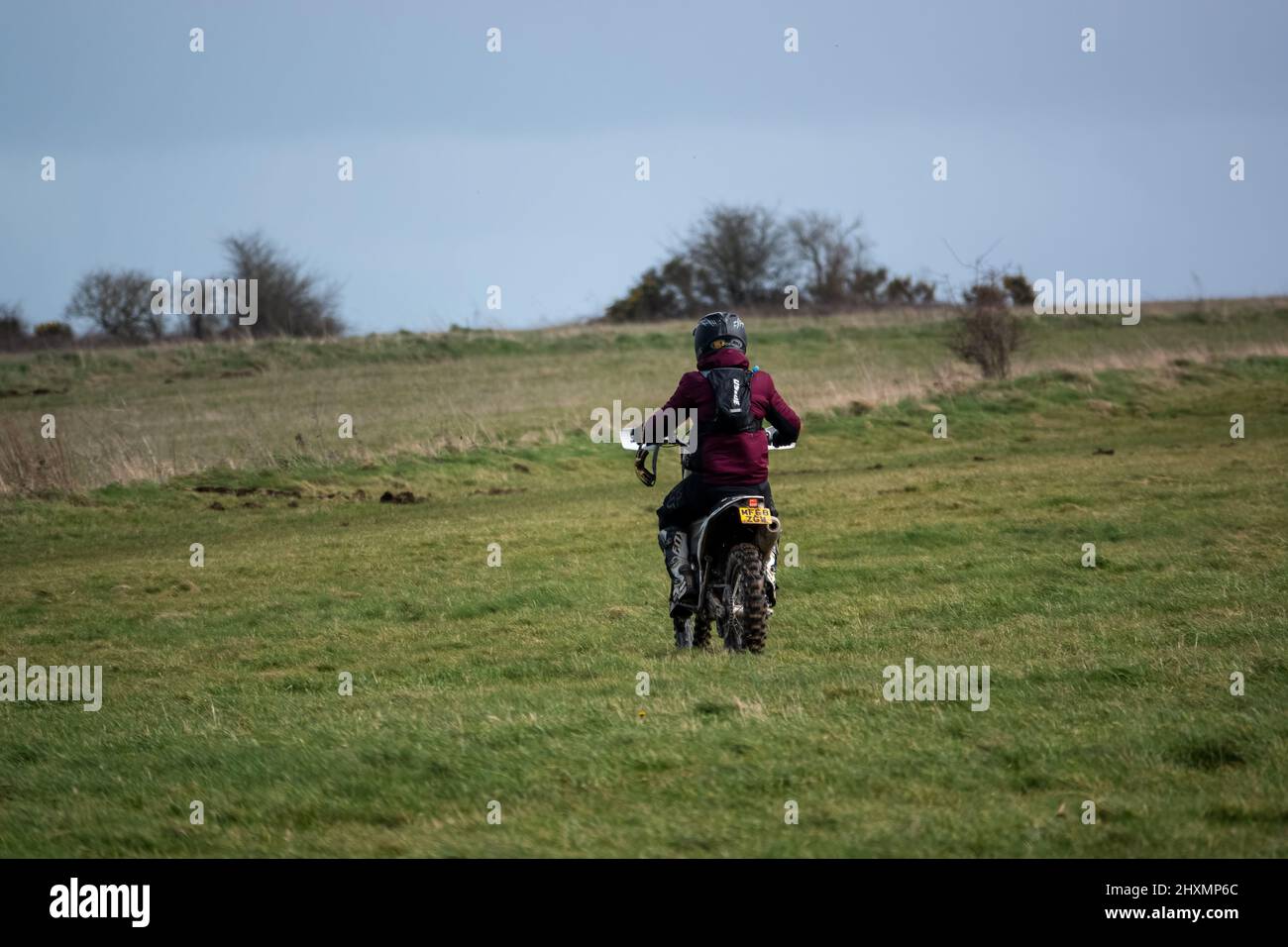 a motor cyclist (biker) riding his off-road motorbike across green ...