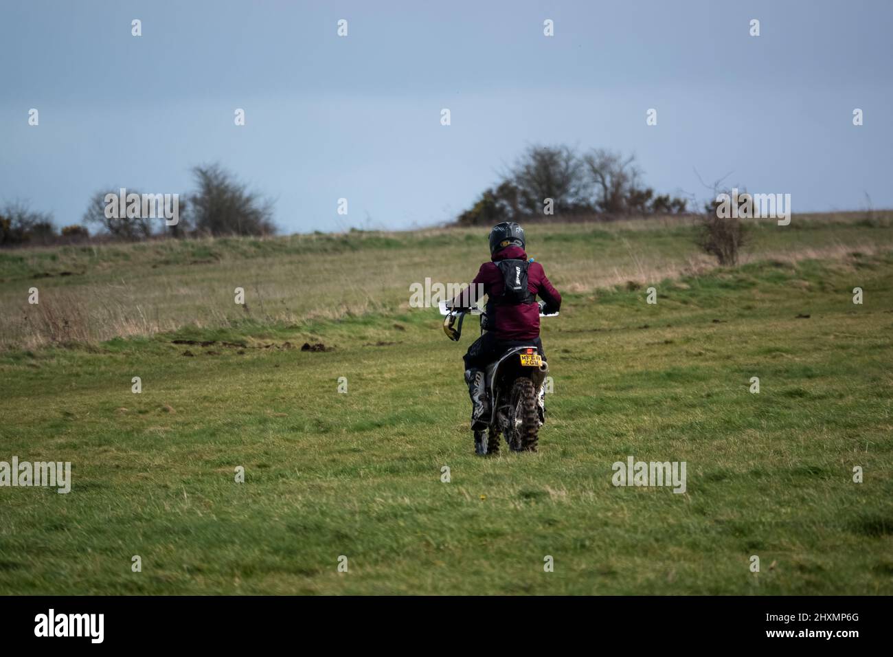 a motor cyclist (biker) riding his off-road motorbike across green ...