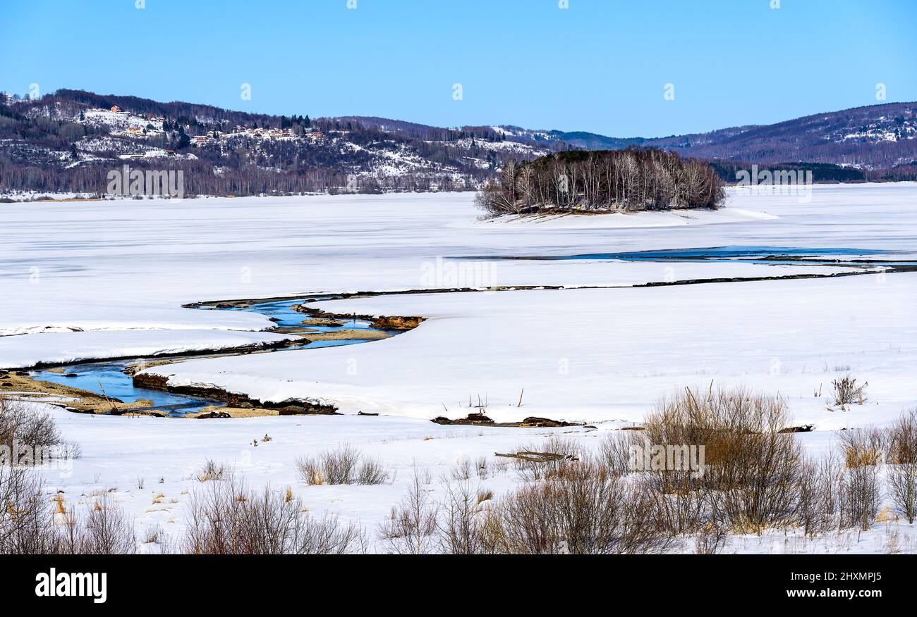 Winter landscape with a tributary River entering the frozen lake with ...