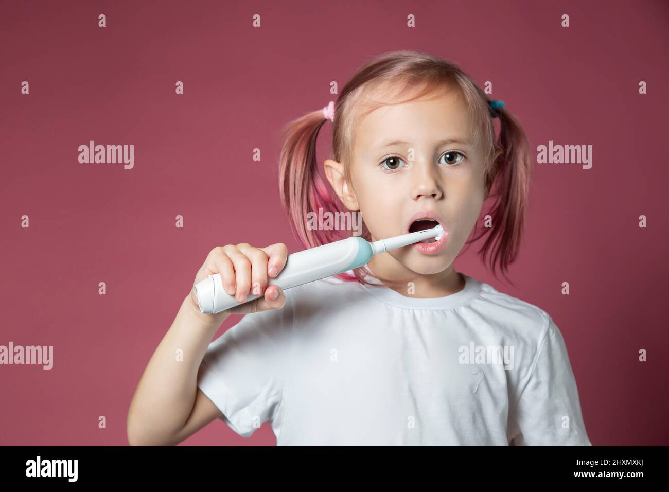 Smiling caucasian little girl cleaning his teeth with electric sonic ...
