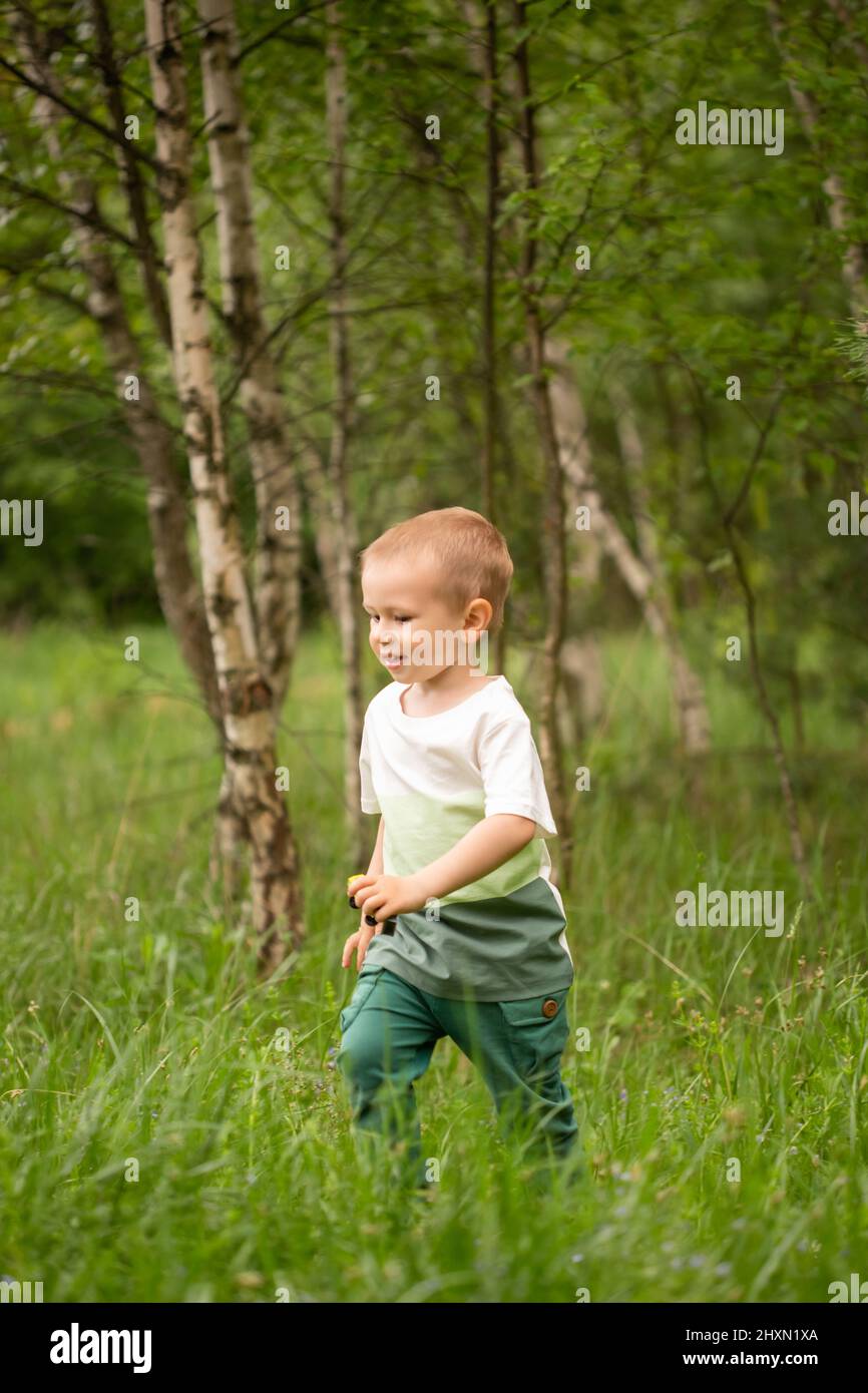 Cute Caucasian boy in the forest against the background of grass summertime Stock Photo - Alamy