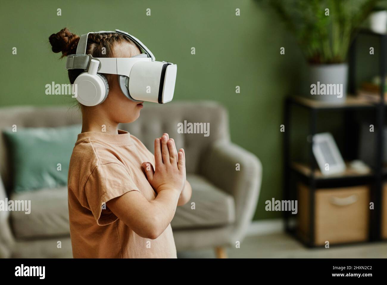 Side view portrait of tween girl practicing yoga workout in VR at home ...