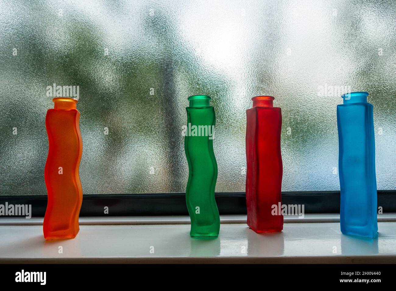Colourful glass vases sat on a window ledge Stock Photo - Alamy